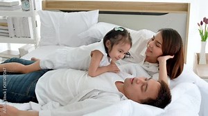 Asian family happy spending time together on the bed in the house. Daughter aged three kissing cheeks parents.
